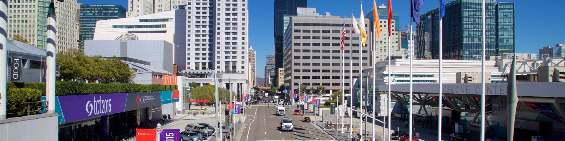 Rua urbana com edifícios altos, bandeiras e carros.