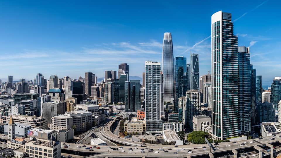 Paisagem urbana com um arranha-céu imponente, edifícios densos e uma ponte sobre a água.