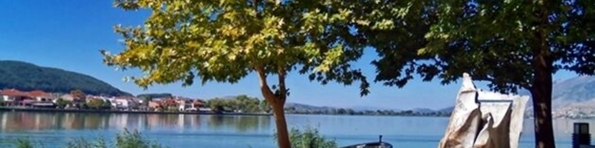 Um lago com barco, árvore e escultura de pedra em base de azulejos.