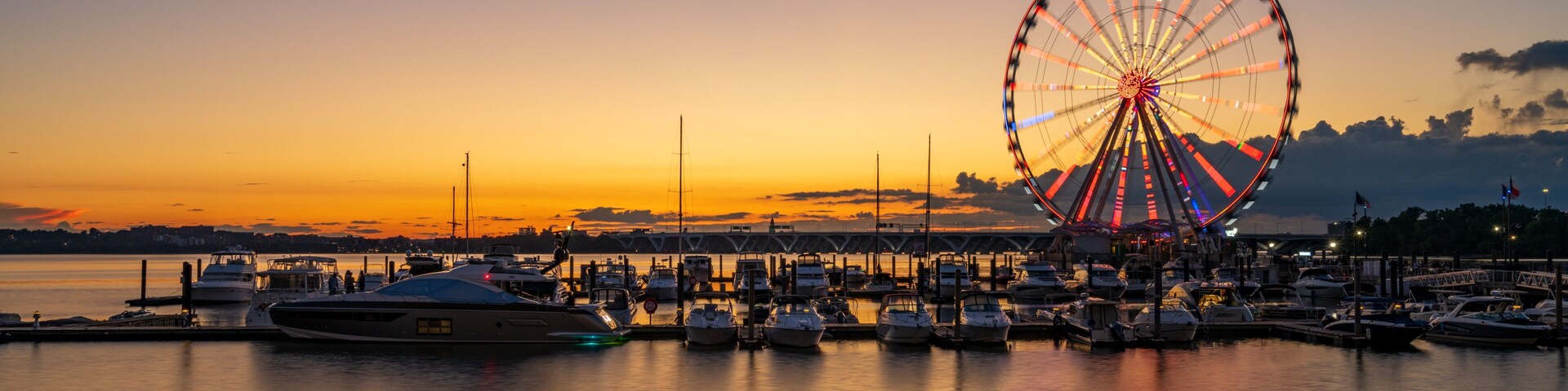 Uma marina ao pôr do sol, com uma grande roda gigante e barcos.