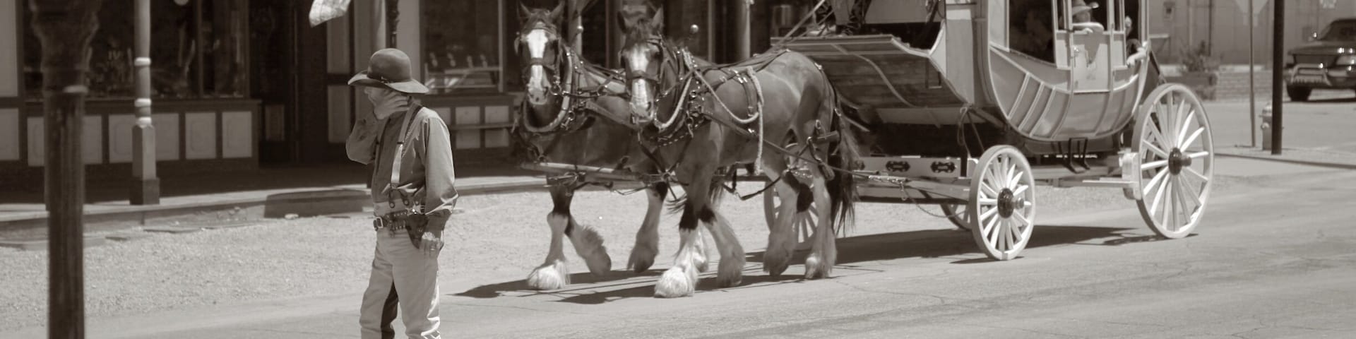 Uma carruagem puxada por cavalos em uma rua, com uma placa indicando 'Miller's Tombstone Mercantile'.