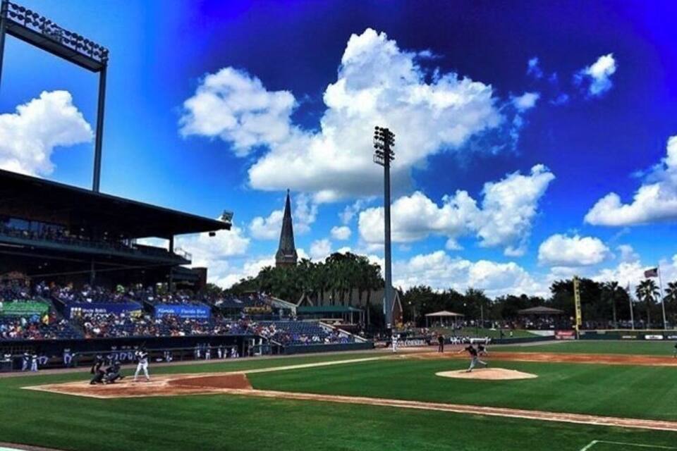 Um estádio de beisebol com céu claro, uma torre e uma multidão de espectadores.