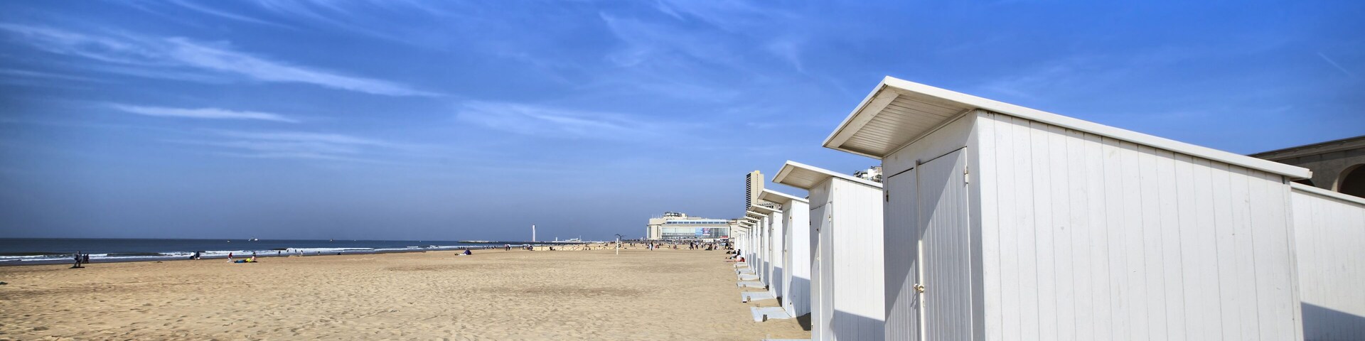 Uma praia arenosa com uma fileira de cabanas de praia brancas sob um céu azul límpido.