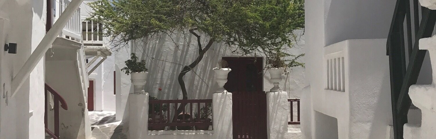 Uma rua estreita de pedra, ladeada por edifícios brancos, com uma torre de sino ao fundo.
