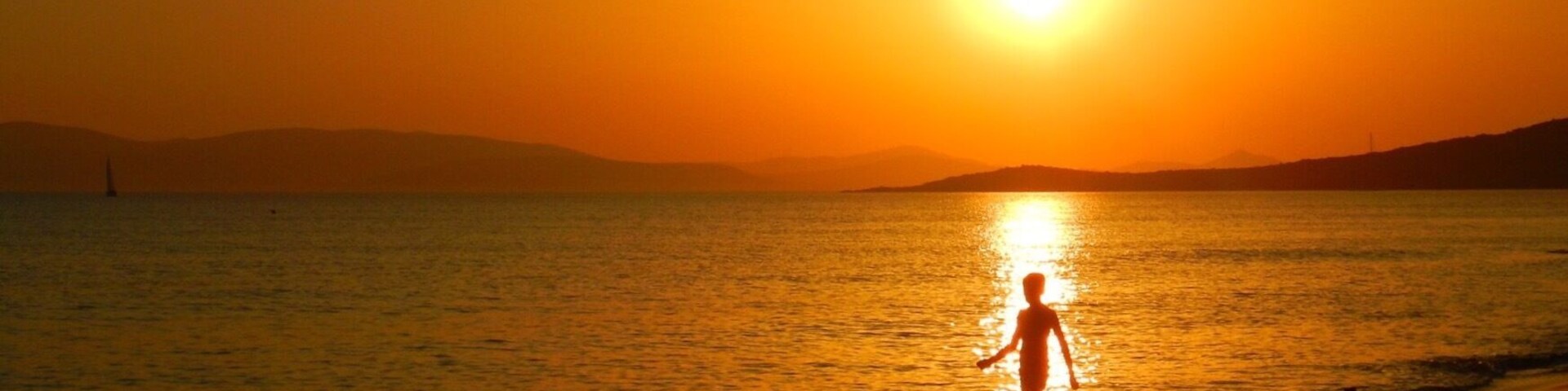 Um pôr do sol sobre um mar calmo, com a silhueta de alguém caminhando na praia.