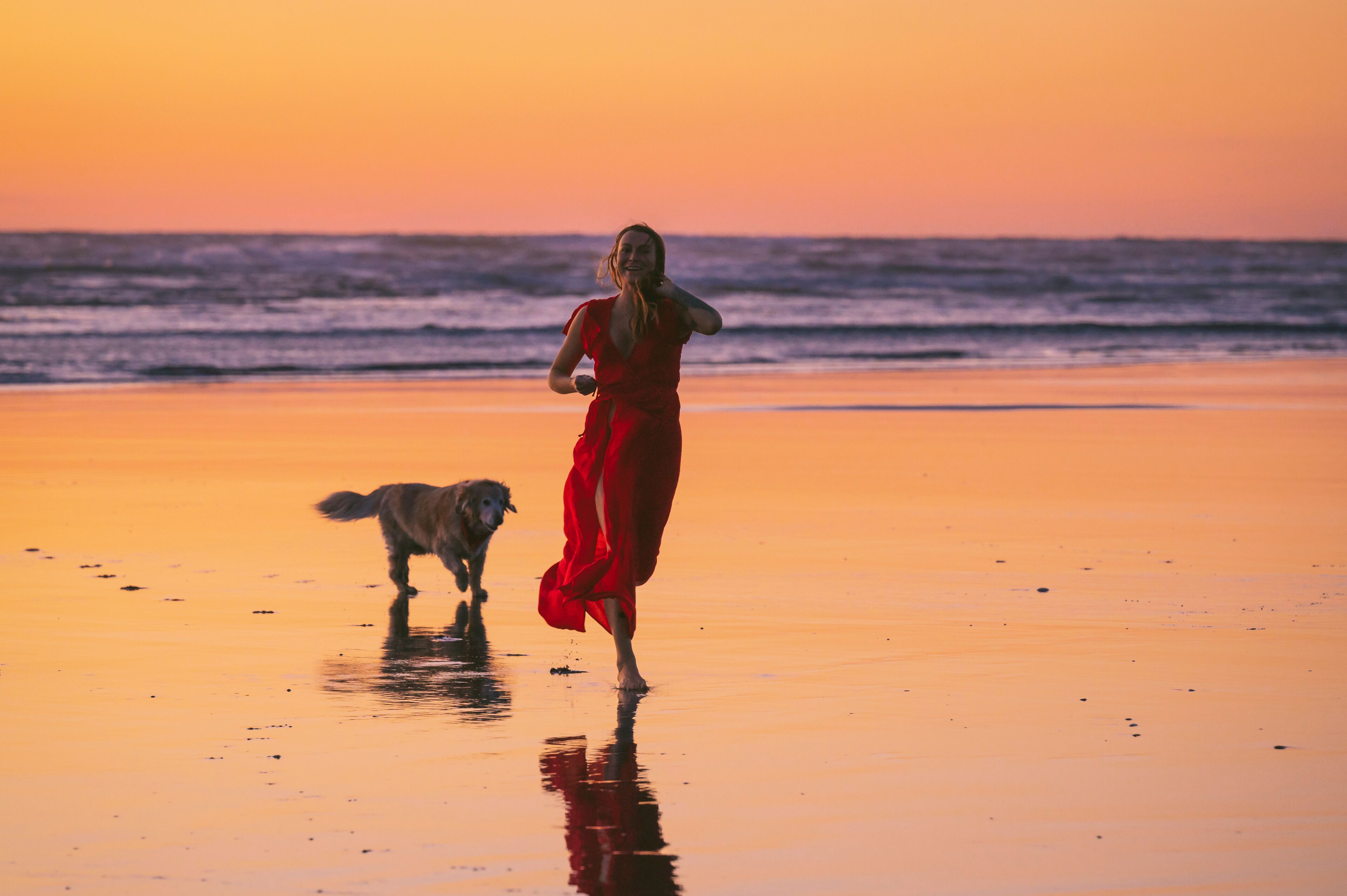 Uma pessoa vestida de vermelho correndo na praia com um cachorro.
