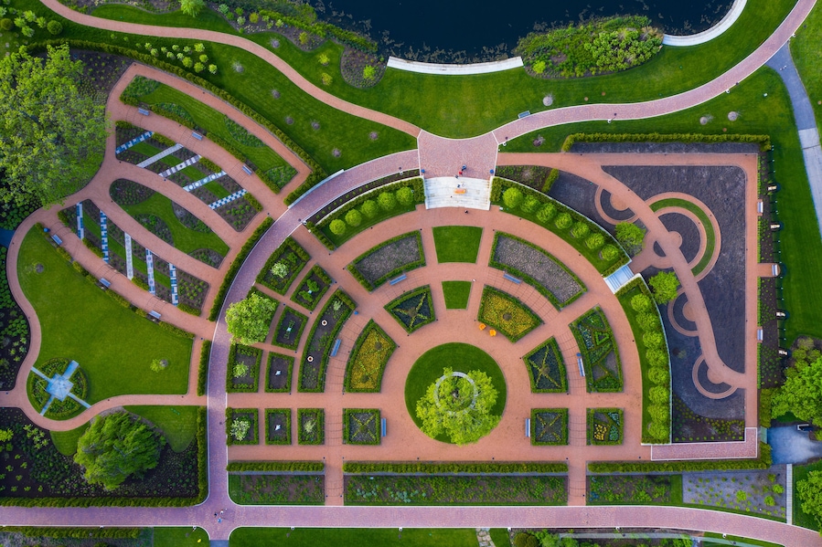 Vista aérea de um parque arborizado com caminhos sinuosos, um jardim circular central e uma fonte.