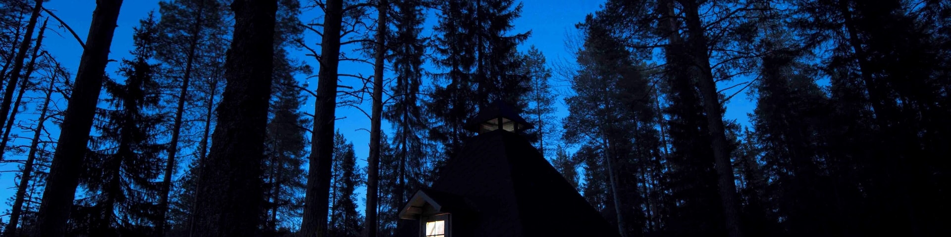 Uma cabana numa floresta ao anoitecer.