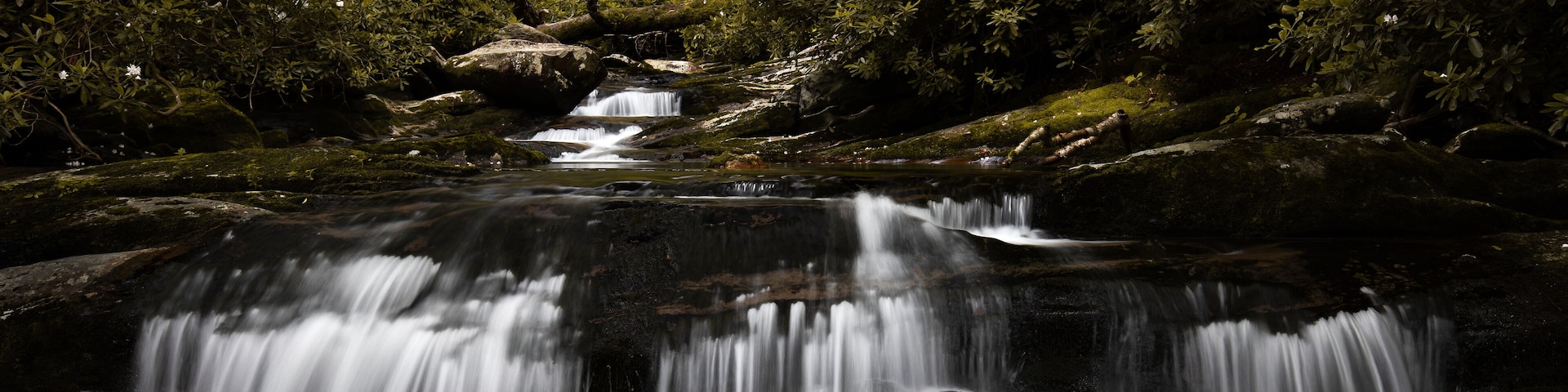 Uma cascata despencando sobre rochas em uma área arborizada.