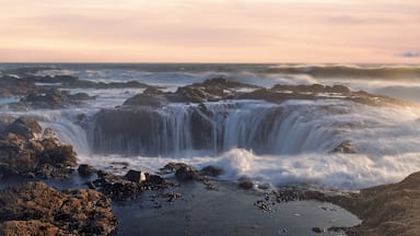 Paisagem costeira com cachoeira, terreno rochoso e ondas do oceano.
