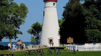 Um farol branco com a parte superior vermelha, rodeado por árvores e uma cerca branca de piquete.