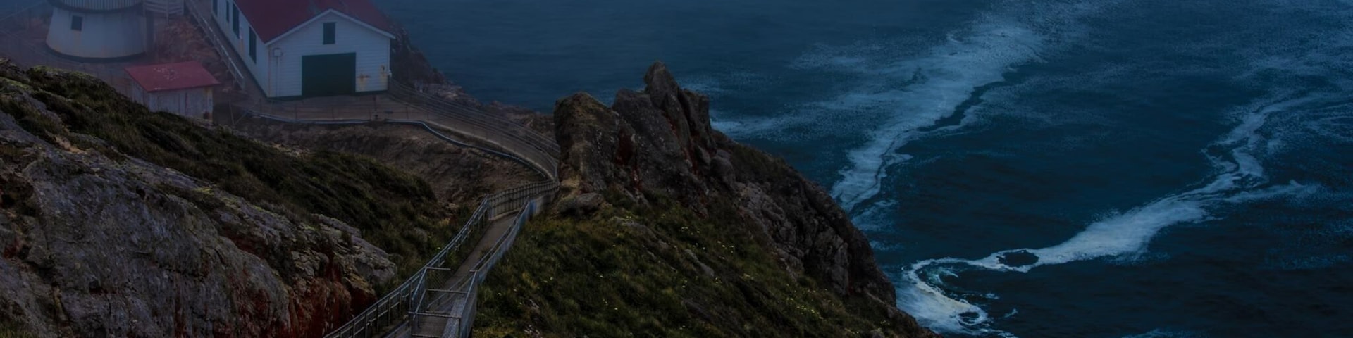 Um farol costeiro e uma escadaria de madeira que desce em direção ao mar.