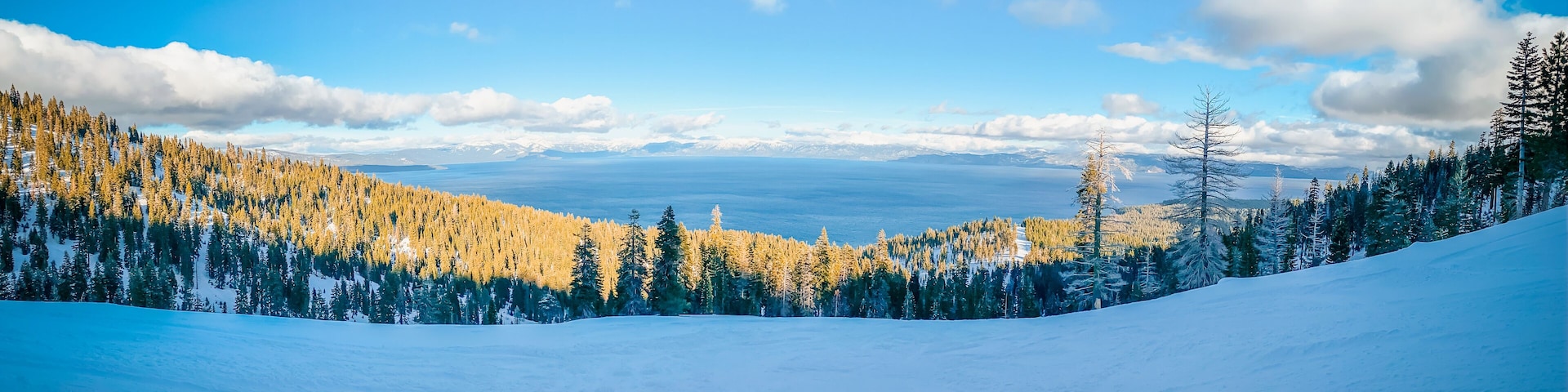 Paisagem montanhosa coberta de neve, com céu claro e montanhas ao longe.