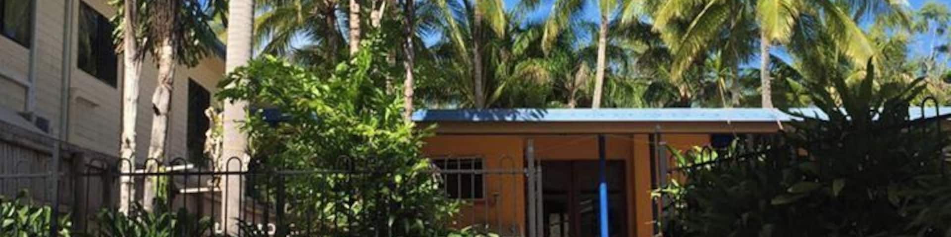 Uma piscina com uma pessoa relaxando em um flutuador, cercada por palmeiras e um edifício.