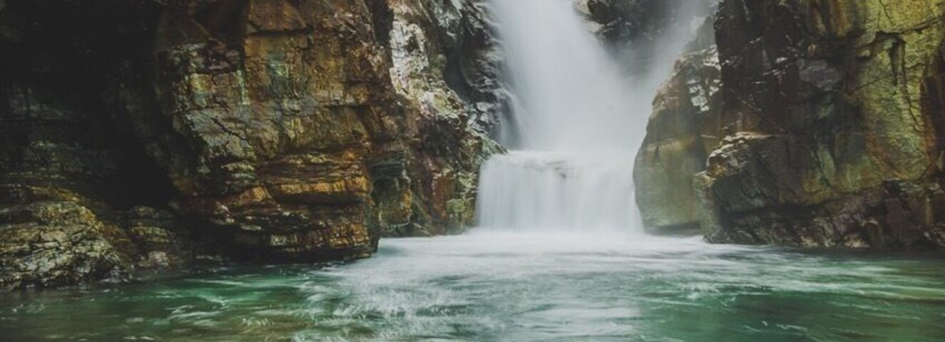 Uma cascata despencando em um rio límpido, cercada por penhascos rochosos e densa floresta.