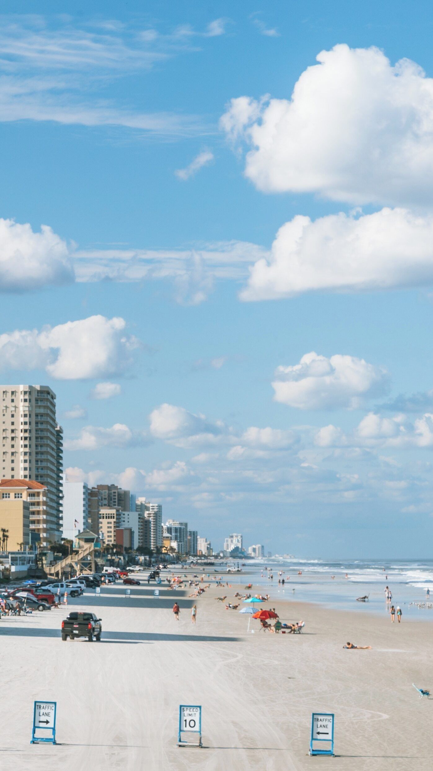 Uma praia com pessoas se banhando e tomando sol, uma placa de limite de velocidade e uma placa de faixa de trânsito.