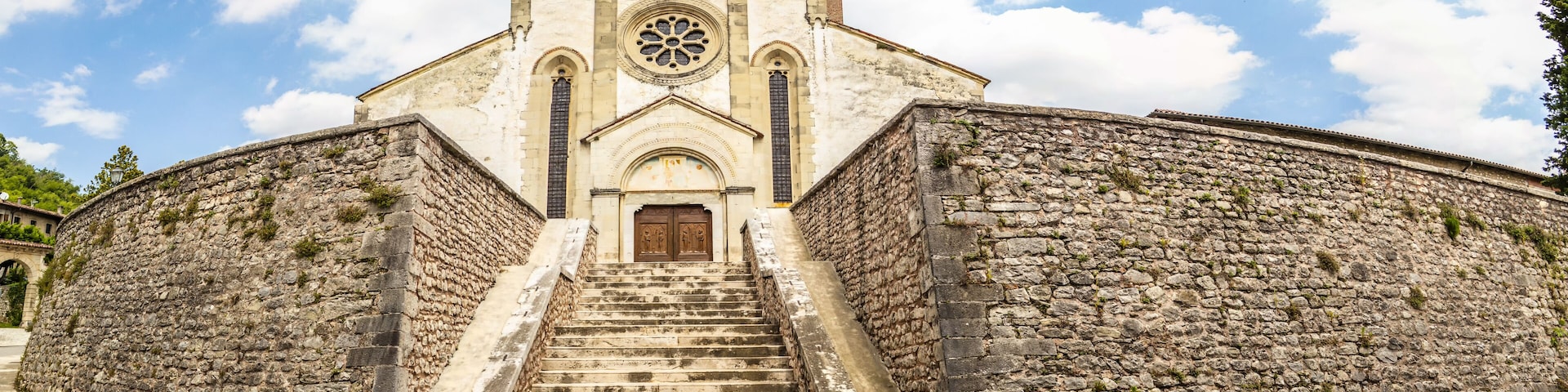 Uma igreja histórica com uma rosácea central, paredes de pedra e uma escadaria que leva à entrada.