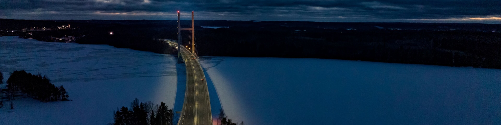 Uma ponte coberta de neve ao crepúsculo, com veículos passando.