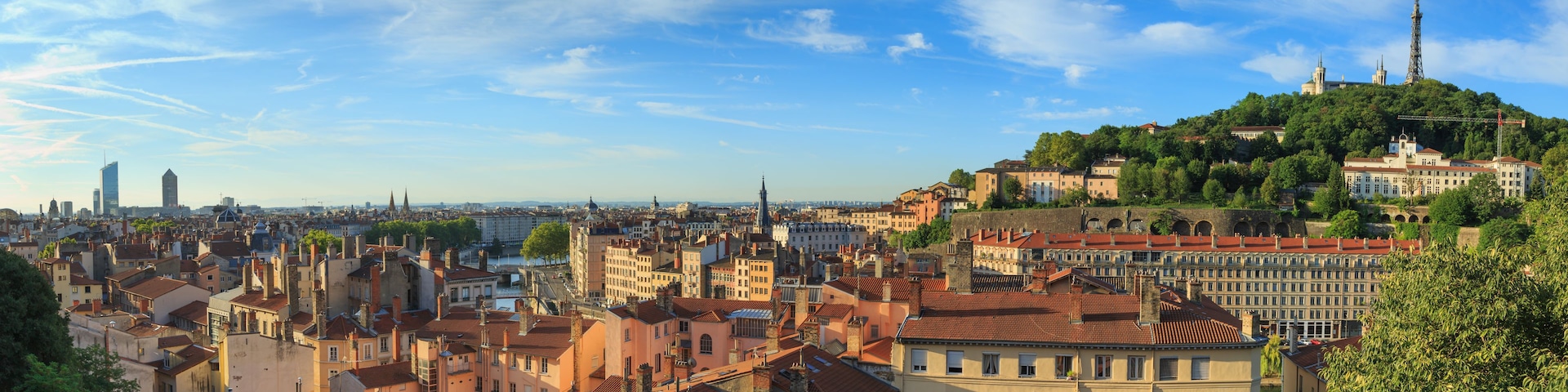 Vista panorâmica de uma cidade com arquitetura histórica, uma igreja imponente no topo de uma colina e um rio ao primeiro plano.