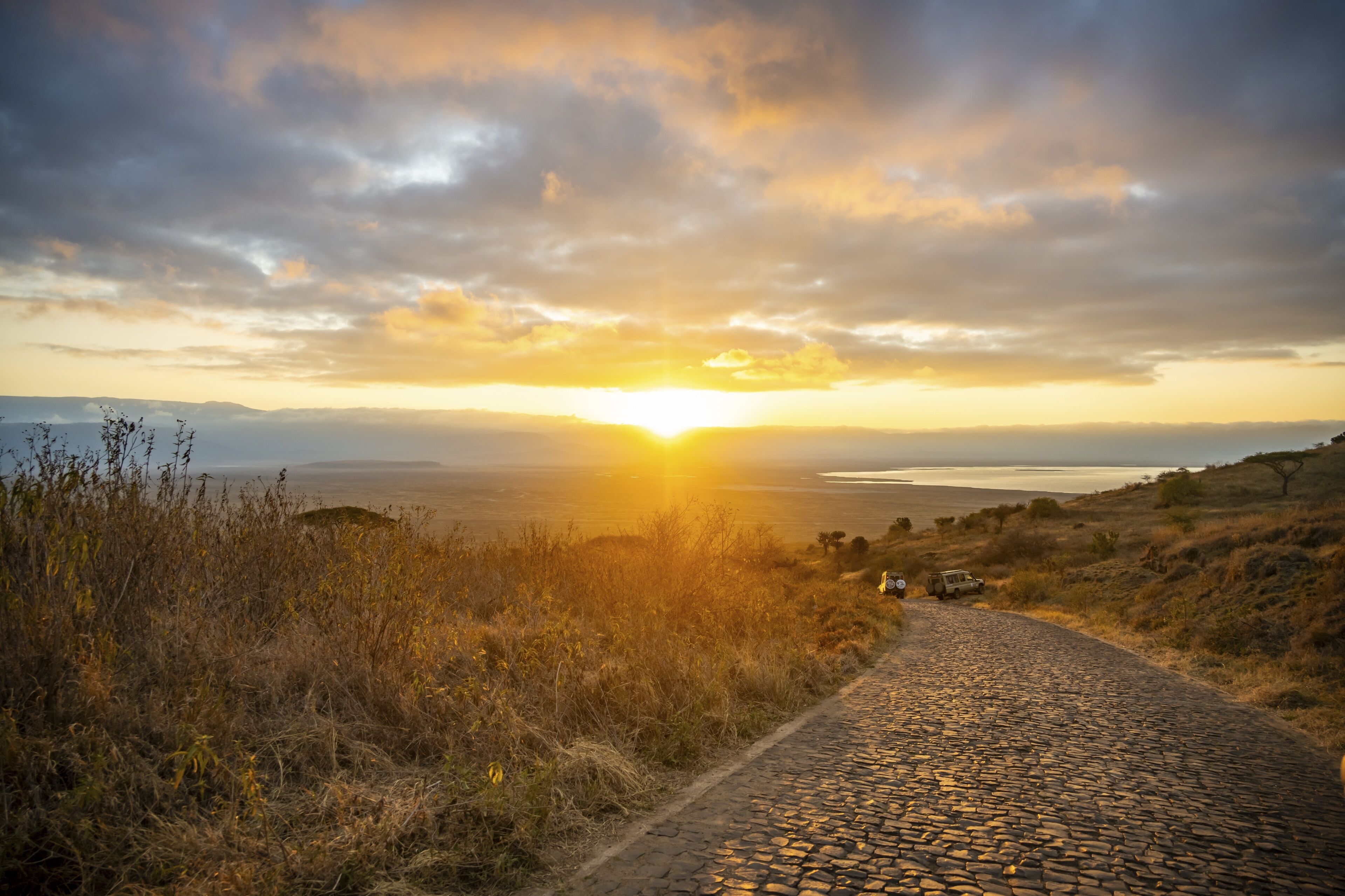 Uma rua de paralelepípedos que leva a um pôr do sol refletido na água.