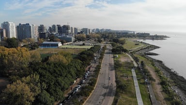 Vista aérea de uma cidade costeira com arranha-céus, um parque e um calçadão à beira-mar.