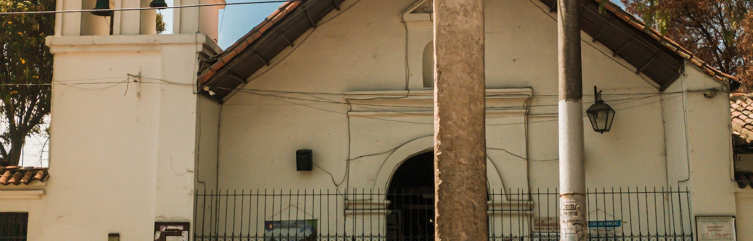 Igreja com um campanário e uma grande cruz de pedra à frente.