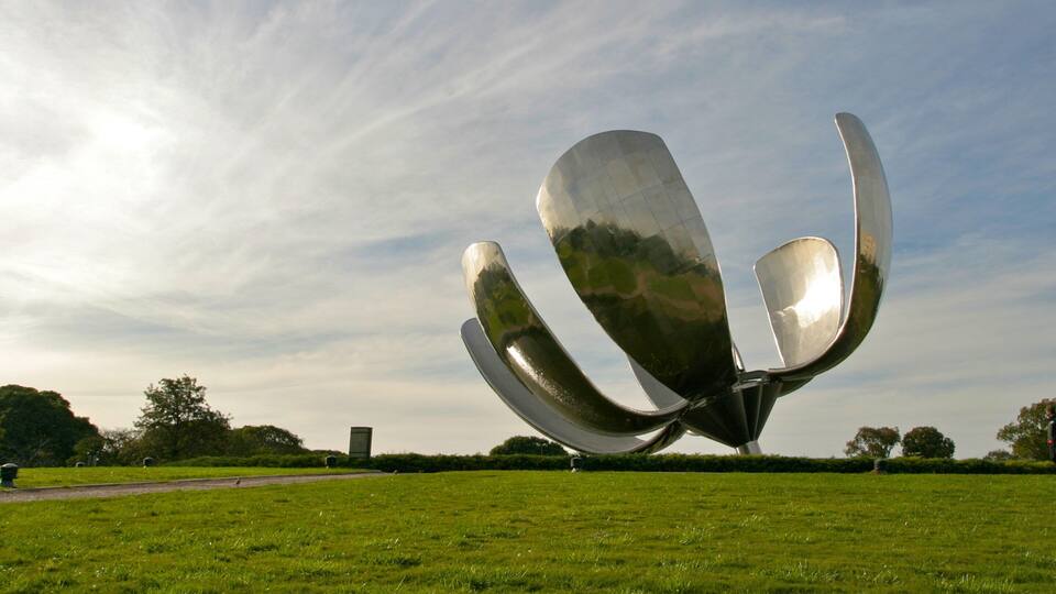 Uma grande escultura metálica em um campo gramado sob um céu claro.