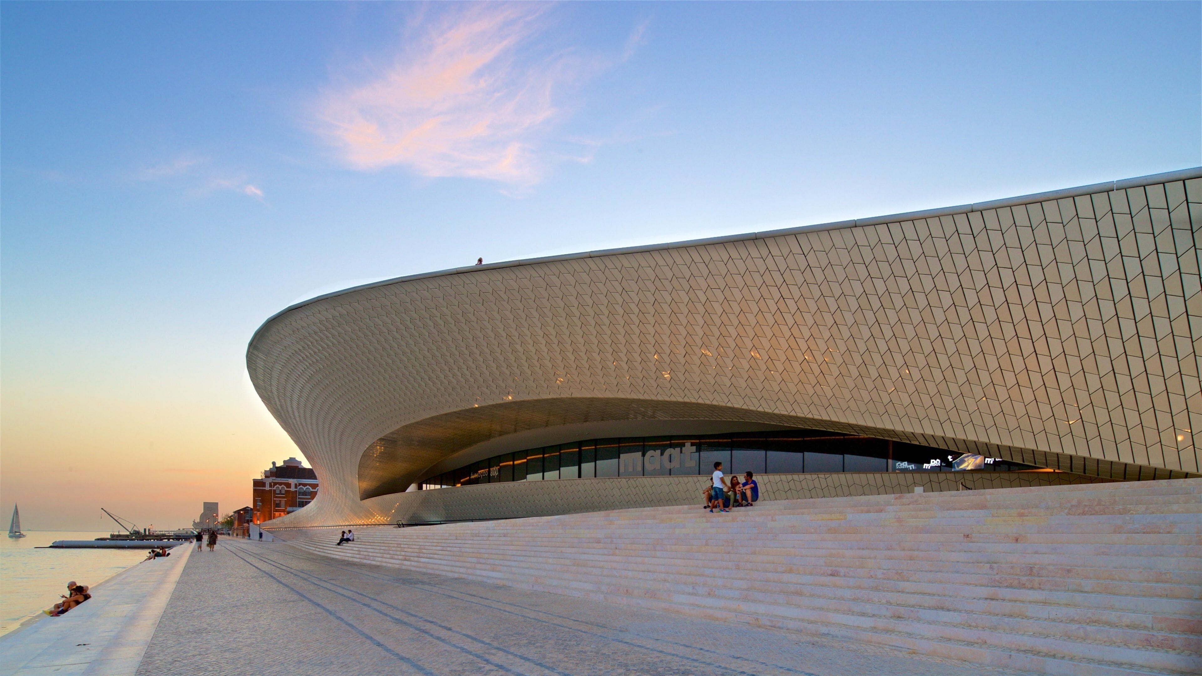 Um edifício moderno com design curvo próximo a uma orla marítima.