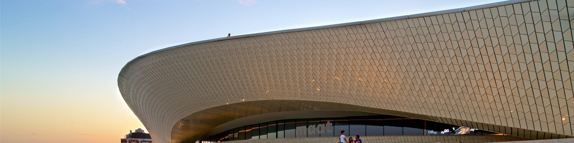 Um edifício moderno com design curvo próximo a uma orla marítima.