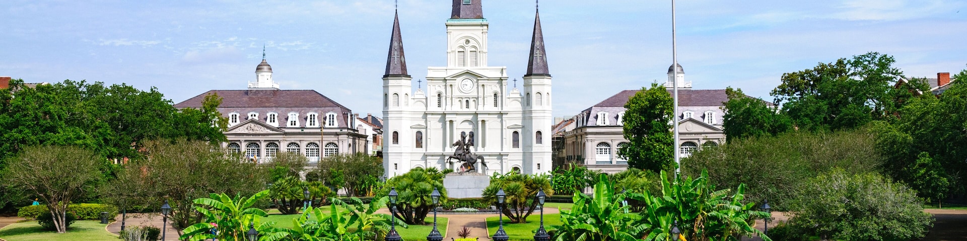 Uma igreja histórica com três torres, cercada por vegetação exuberante e um mastro com a bandeira americana.