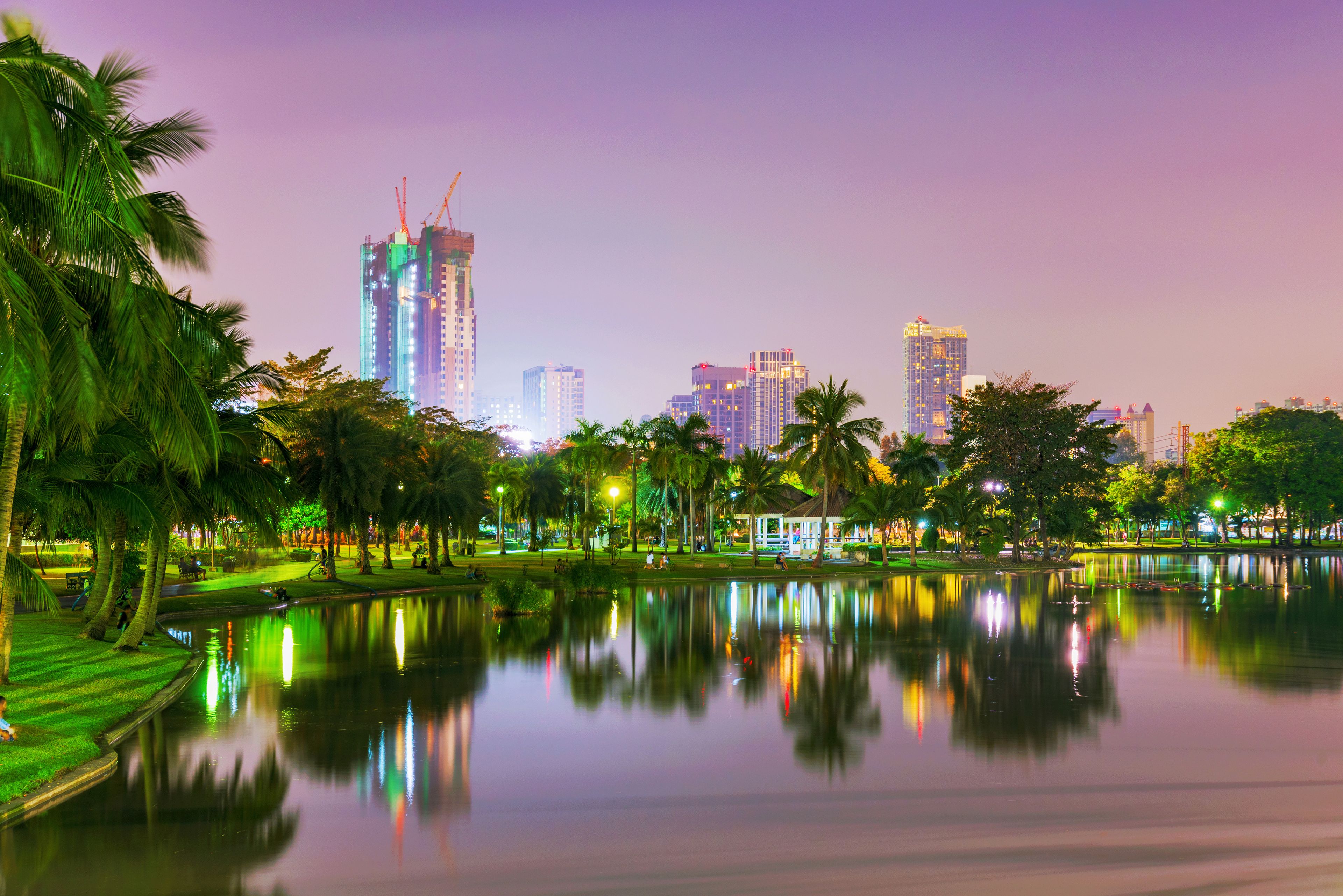 Um lago sereno reflete edifícios da cidade e palmeiras ao anoitecer.