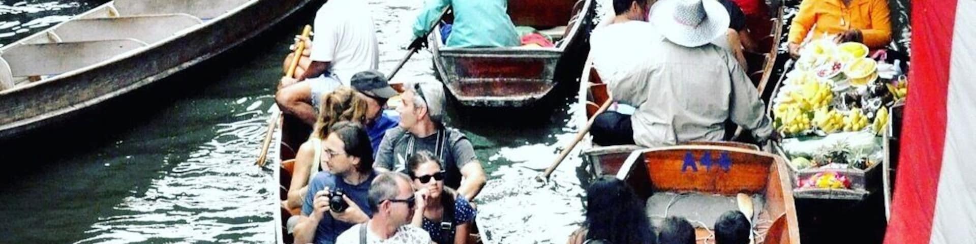 Um canal movimentado com barcos pequenos cheios de pessoas e vendedores oferecendo produtos.