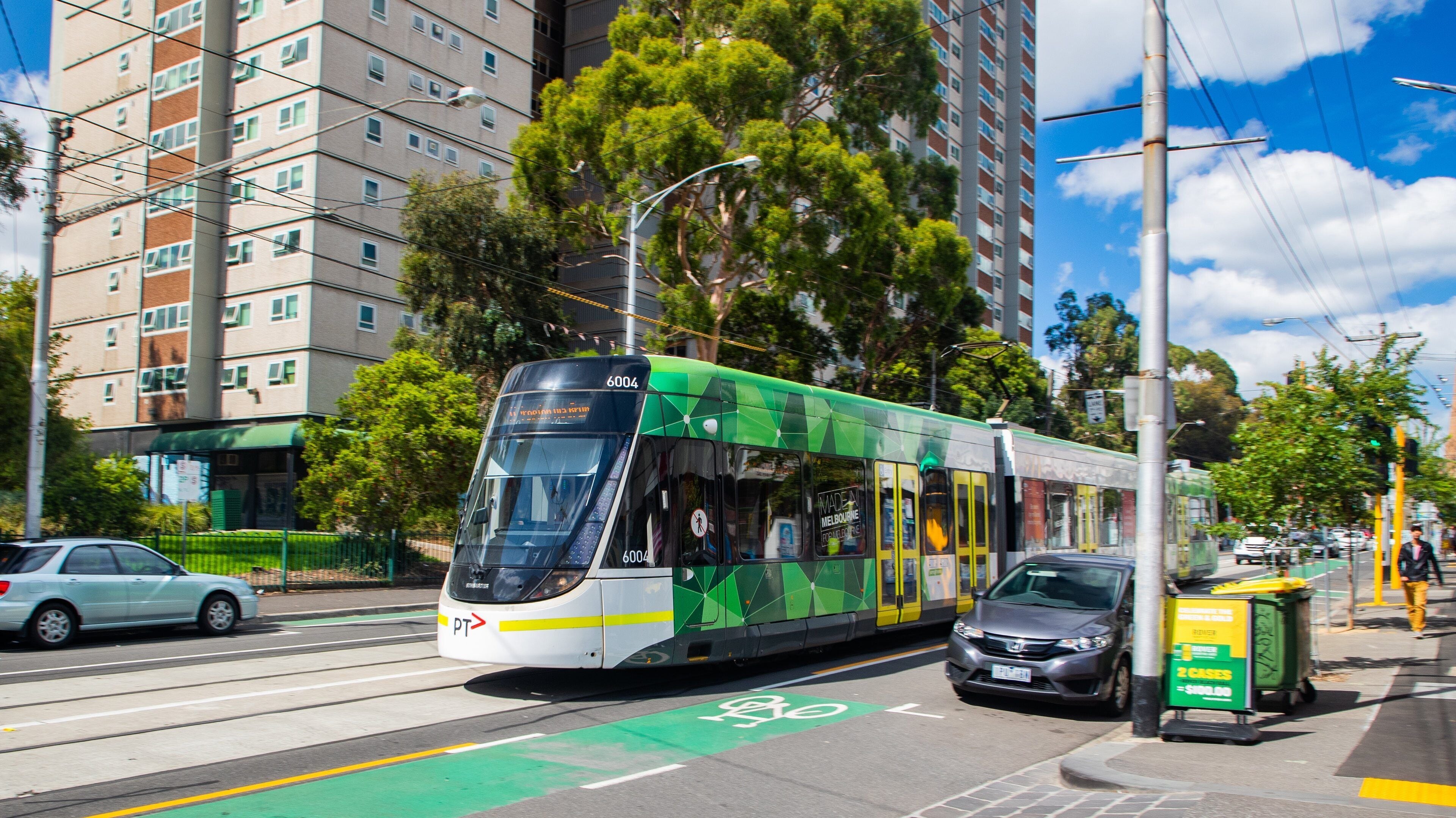 Um eléctrico verde e branco numa rua da cidade, com edifícios e árvores ao fundo.