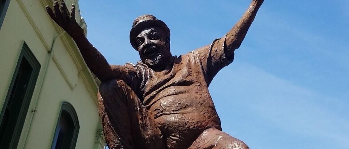 Uma estátua de bronze de um homem com os braços estendidos sobre um pedestal, com um cartaz anunciando eventos de lançamento da EP.
