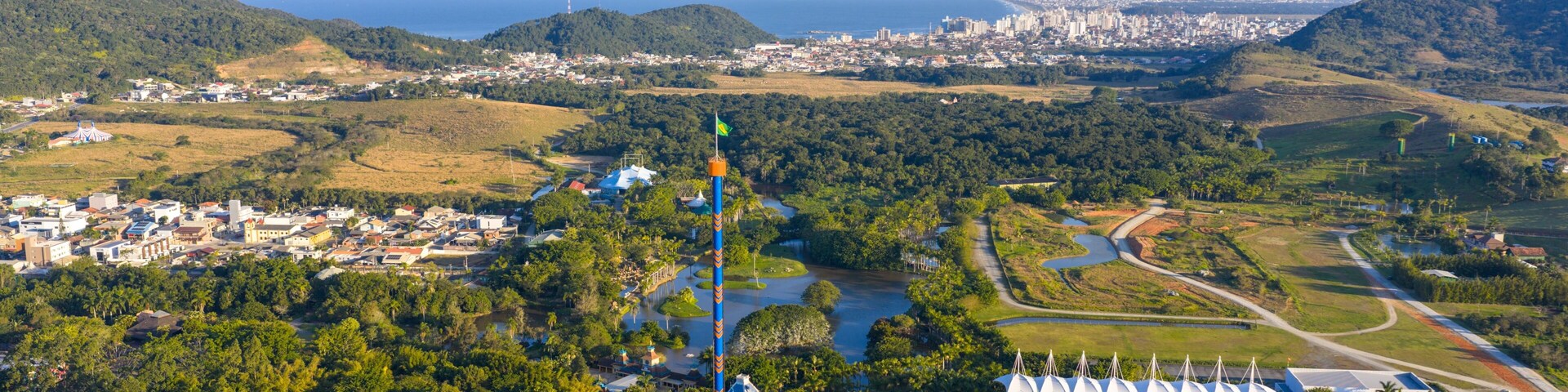 Paisagem costeira com parque temático, rio e horizonte urbano distante.