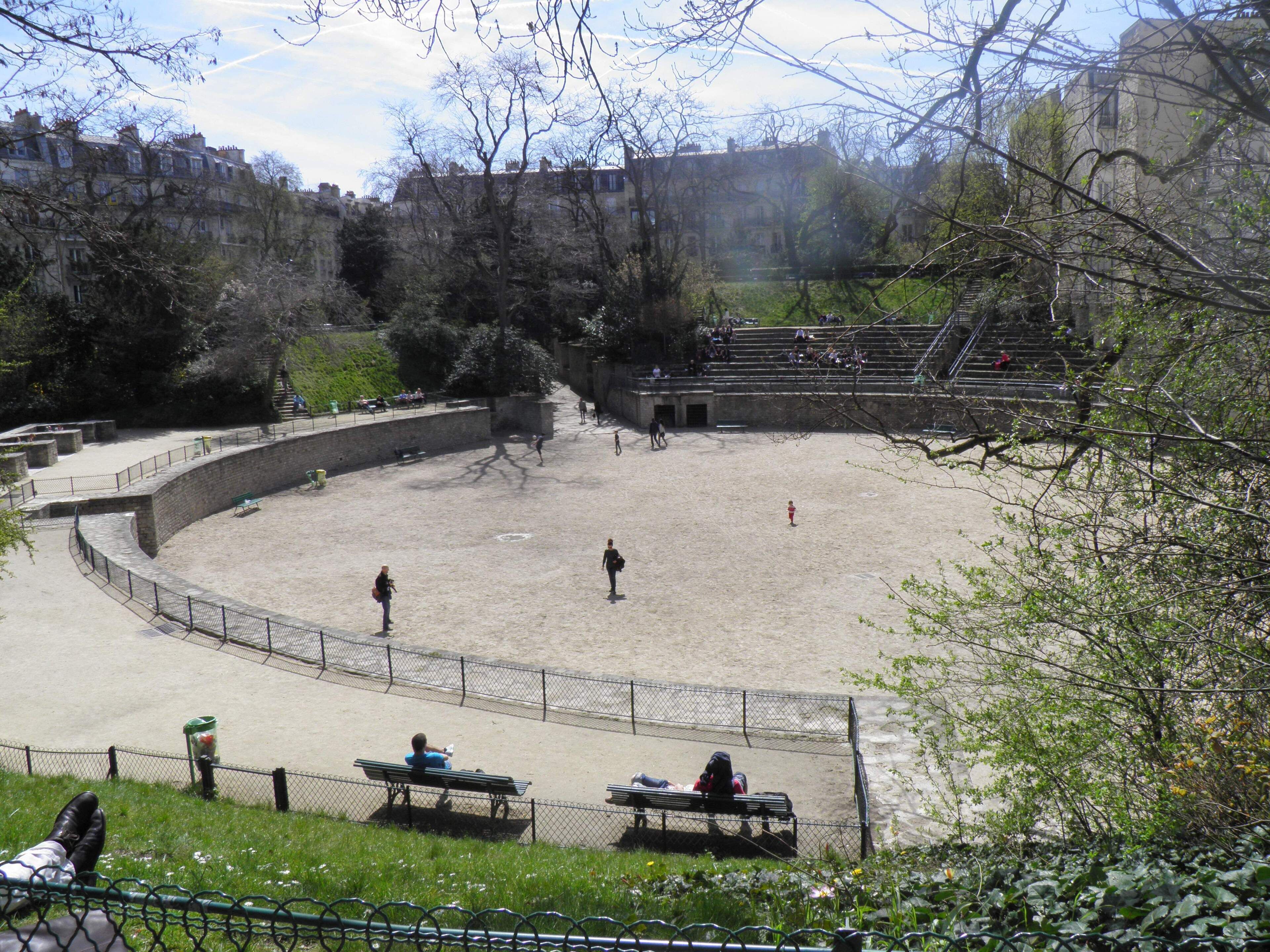 Um campo de esportes arenoso com área de assentos e um muro de pedra.