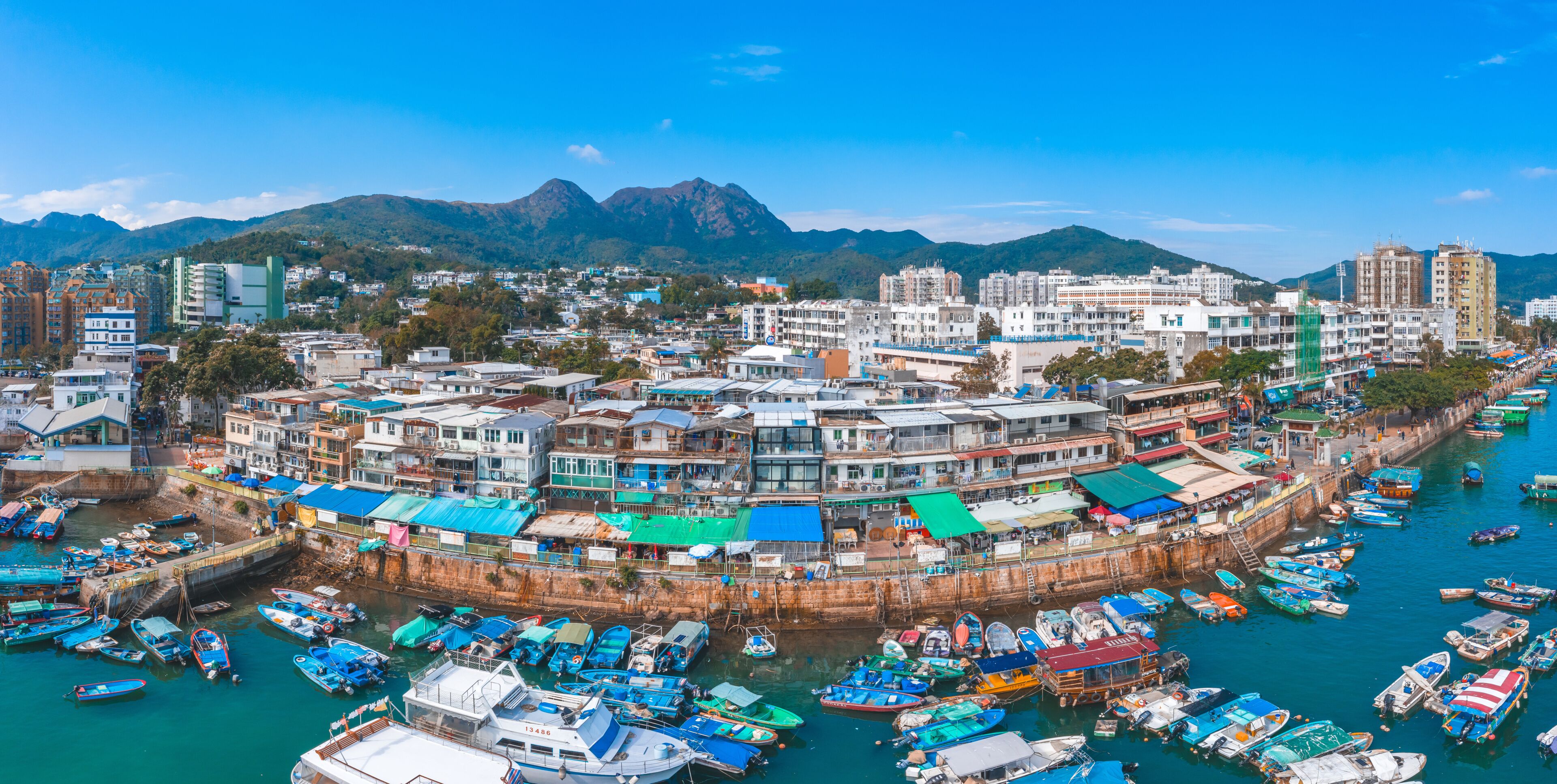 Uma cidade costeira com um conjunto denso de edifícios, um porto cheio de barcos e montanhas ao fundo.