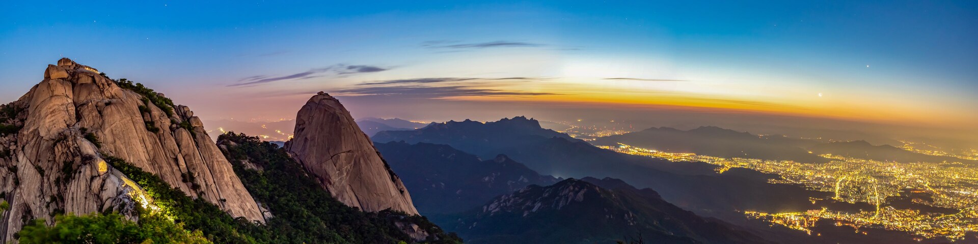 Paisagem montanhosa com um pico imponente e uma cidade iluminada ao fundo.