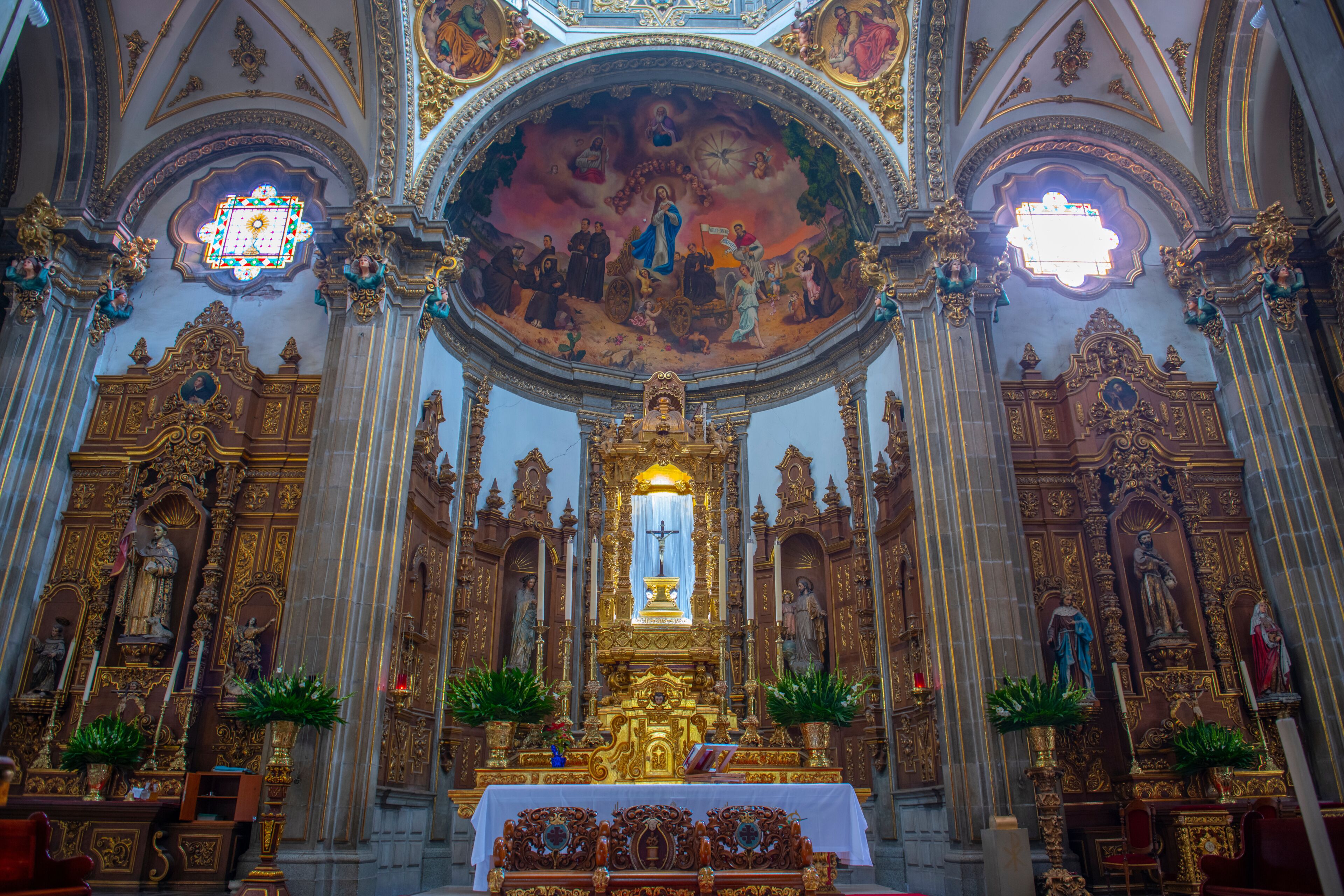 Interior de igreja ornamentado, com altar central, detalhes dourados e pinturas religiosas nas paredes.