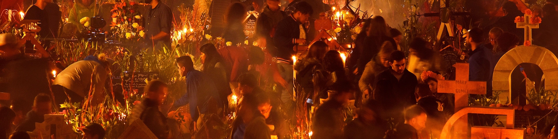 Evento ao ar livre movimentado, com pessoas reunidas em torno de estruturas iluminadas e velas.