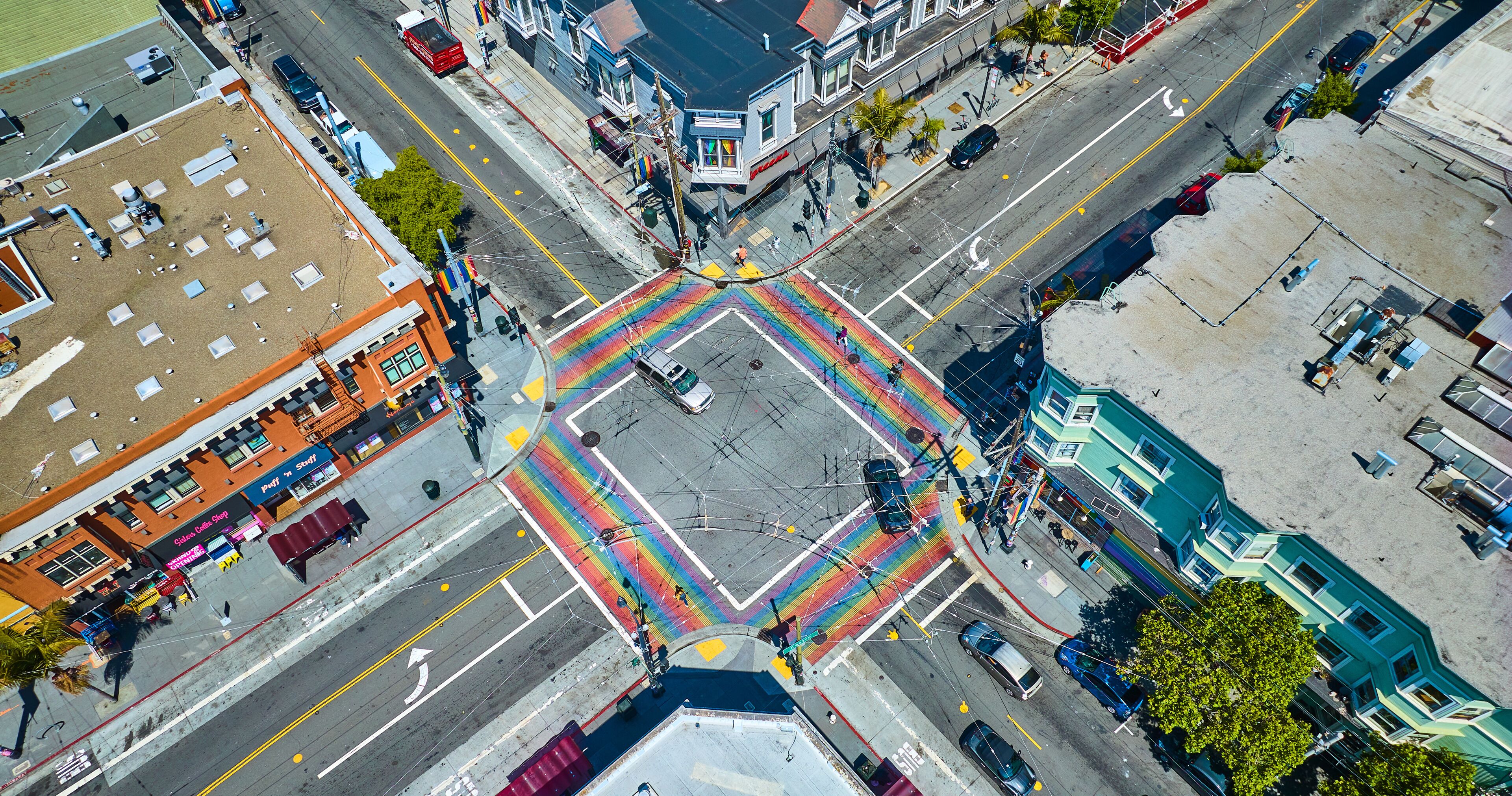 Vista aérea de um cruzamento urbano com uma faixa de pedestres colorida em arco-íris e edifícios ao redor.