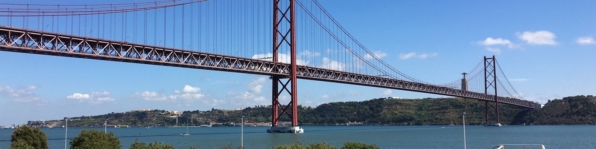 Uma grande ponte suspensa sobre a água, com um parque e trilhos de trem ao primeiro plano.