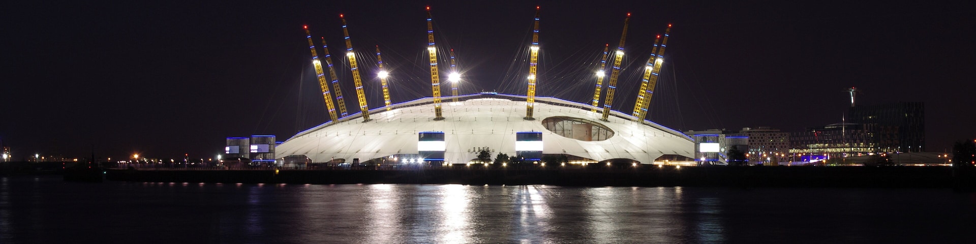 Um estádio grande e iluminado com uma estrutura de teto curva e várias torres de suporte altas.