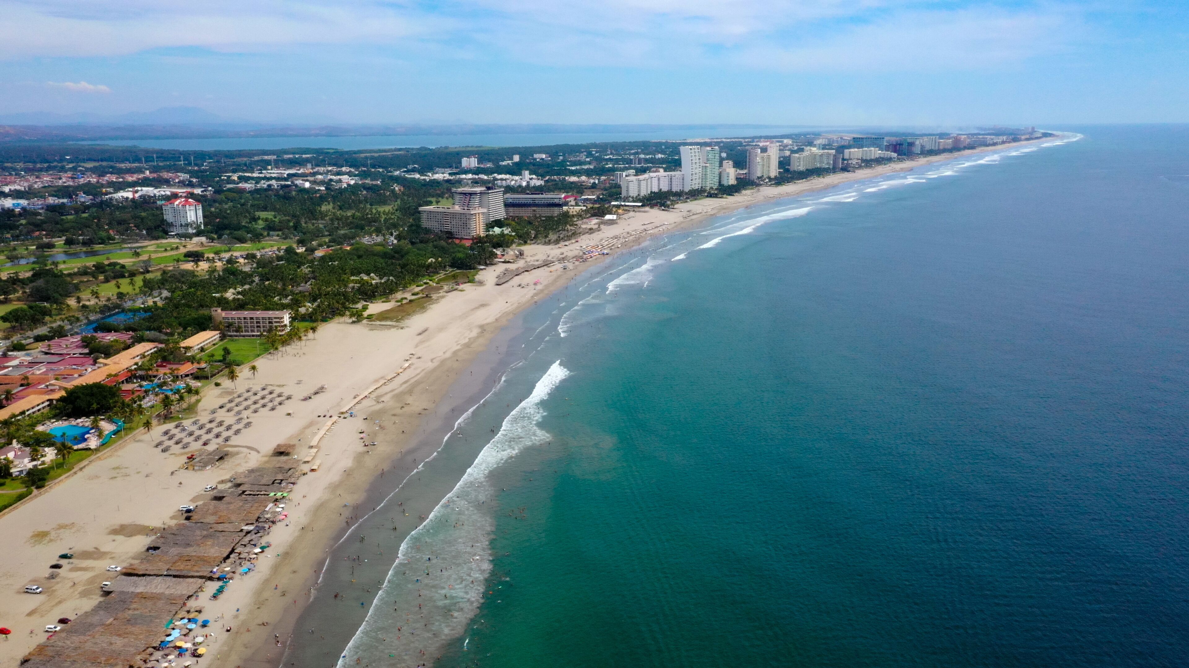 Paisagem costeira com uma praia extensa, edifícios altos e vista clara do oceano.