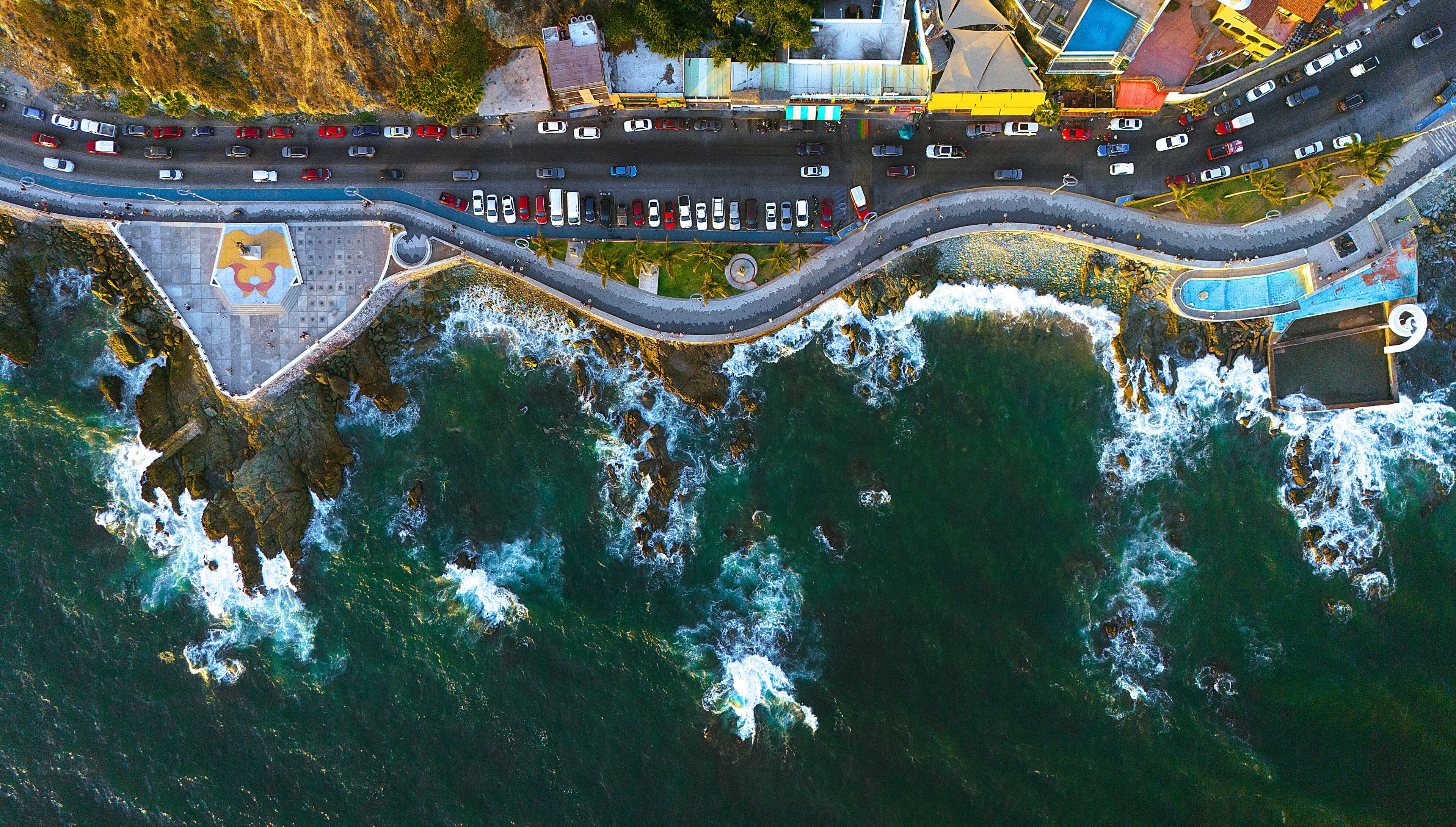 Vista aérea de uma estrada costeira com veículos, praia e edifícios.