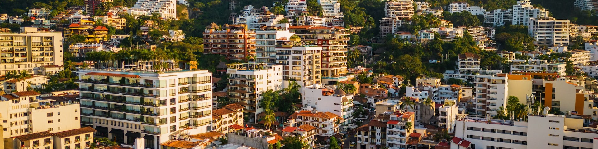 Uma área urbana densamente construída, com mistura de arquitetura moderna e tradicional, rodeada por colinas verdes exuberantes.