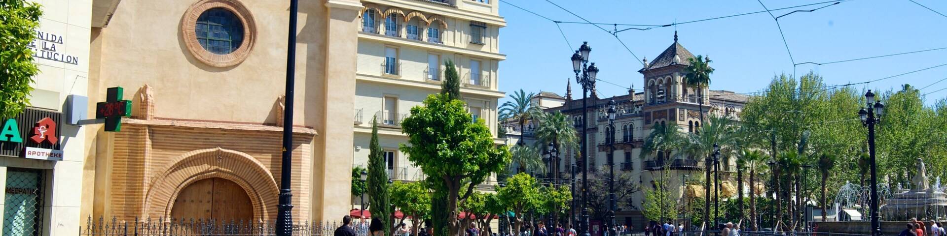 Uma praça urbana ensolarada, com linhas de elétrico, edifícios históricos e pedestres.