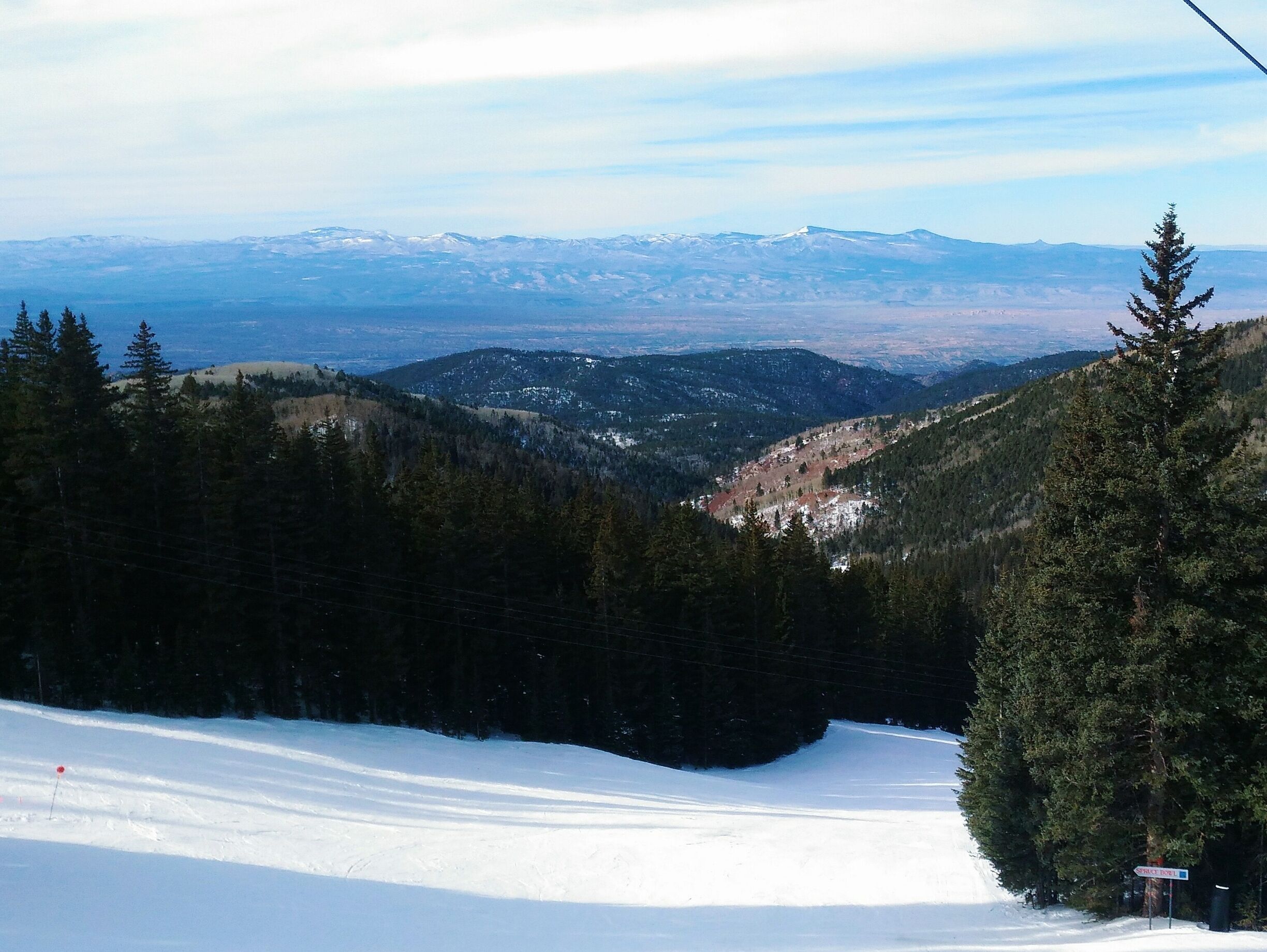 Paisagem montanhosa coberta de neve, com florestas densas e picos nevados ao longe.