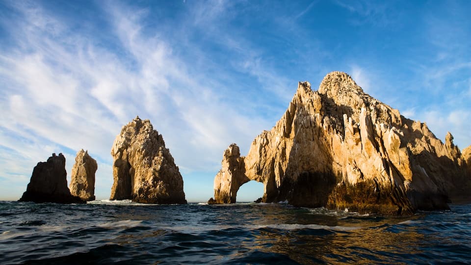 Paisagem costeira com formações rochosas marcantes e um arco sobre o mar.