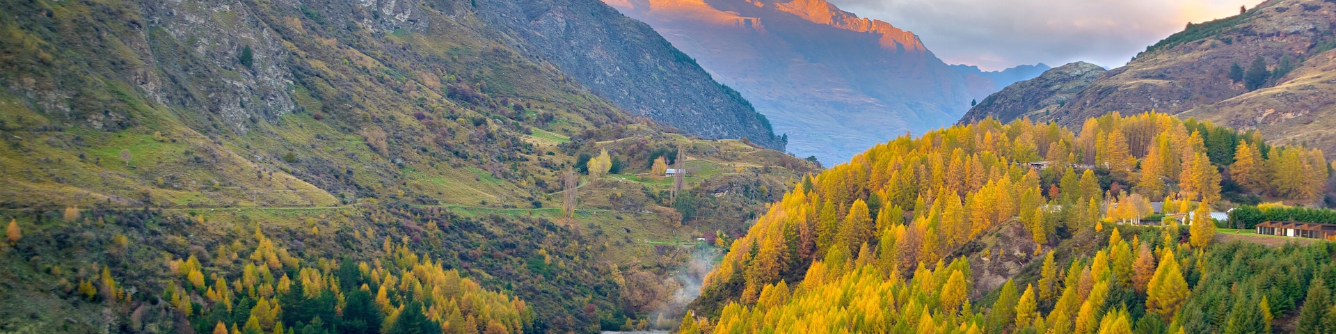 Um rio serpenteando por um vale com árvores de cores outonais e montanhas ao fundo.